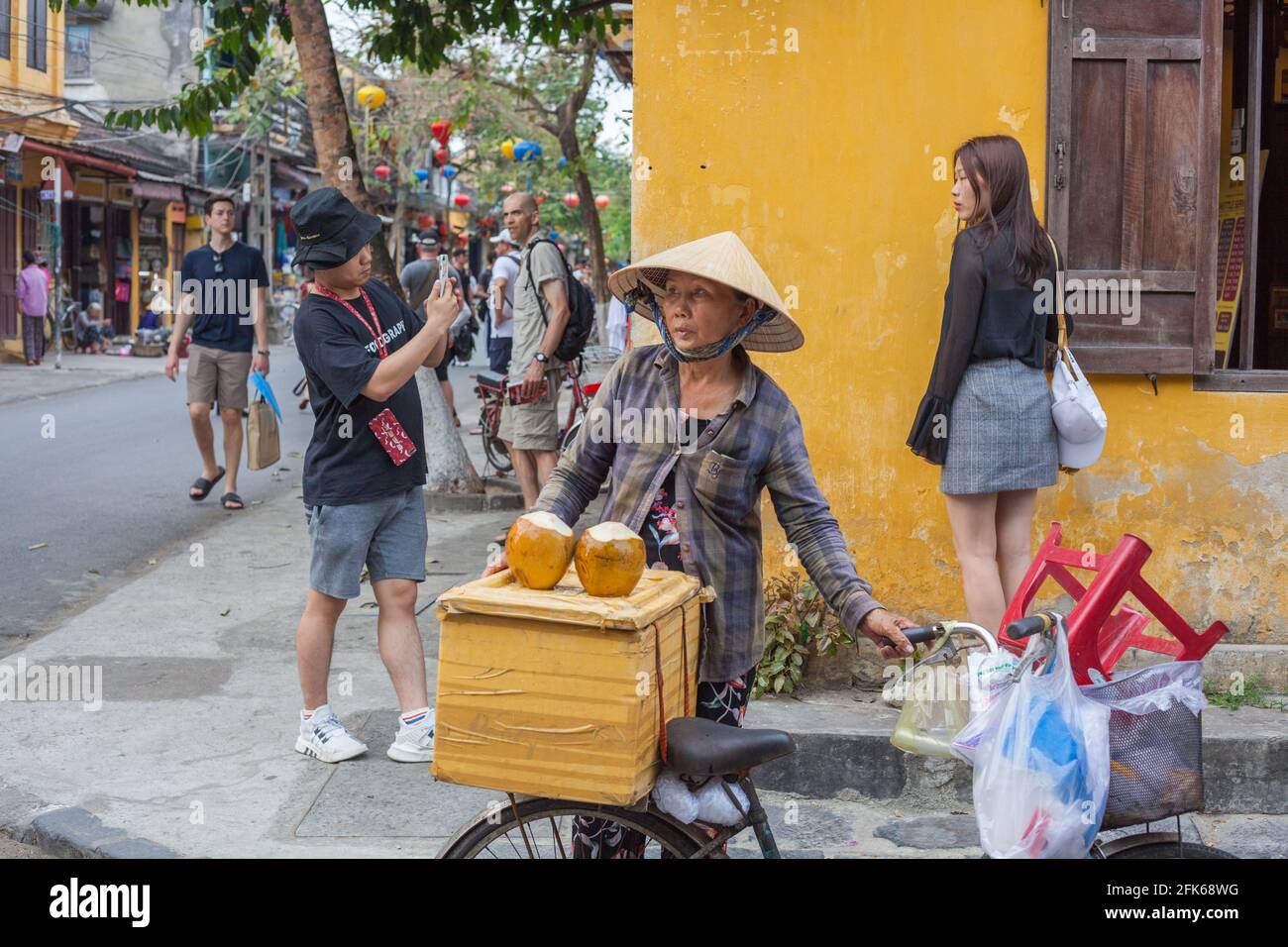 Vietnamese coconut trader selling fruit from her bicycle as tourists ...