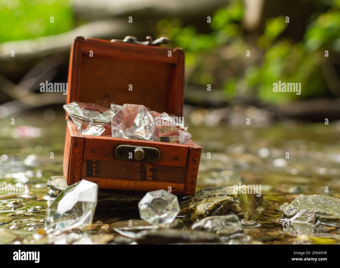 Open wooden box filled to the brim with diamonds on a wet rocky surface ...