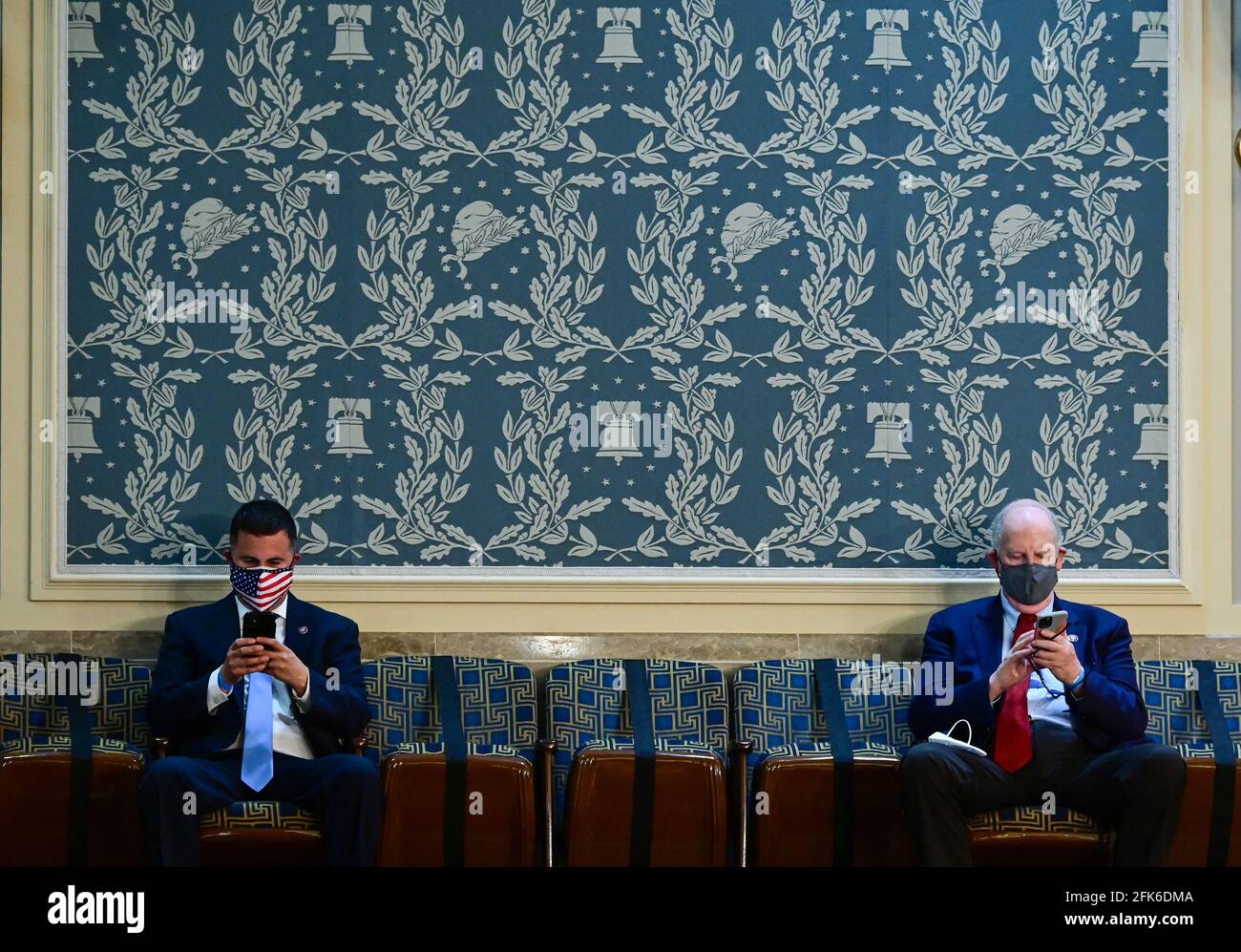 Two members of congress look at their phones as they sit apart ...