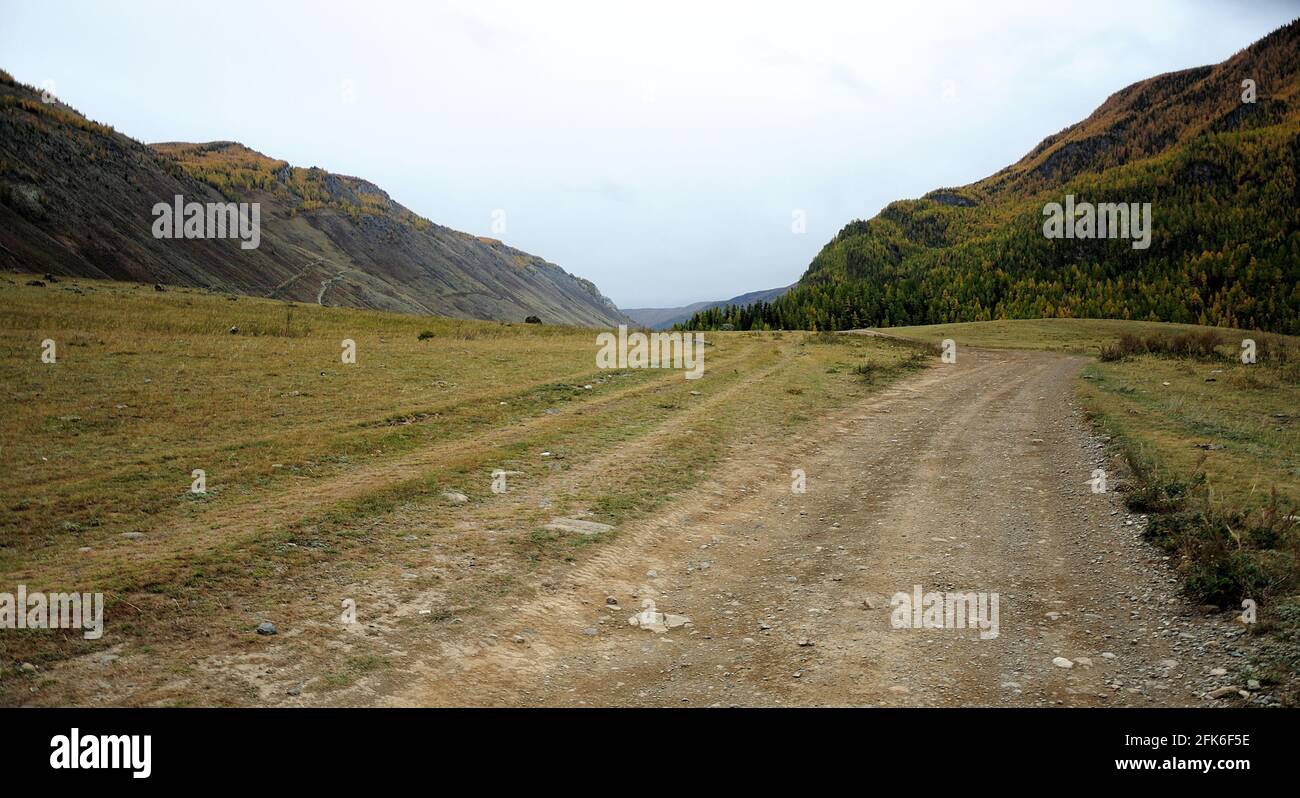 A wide field road going through a gorge surrounded by mountain peaks ...