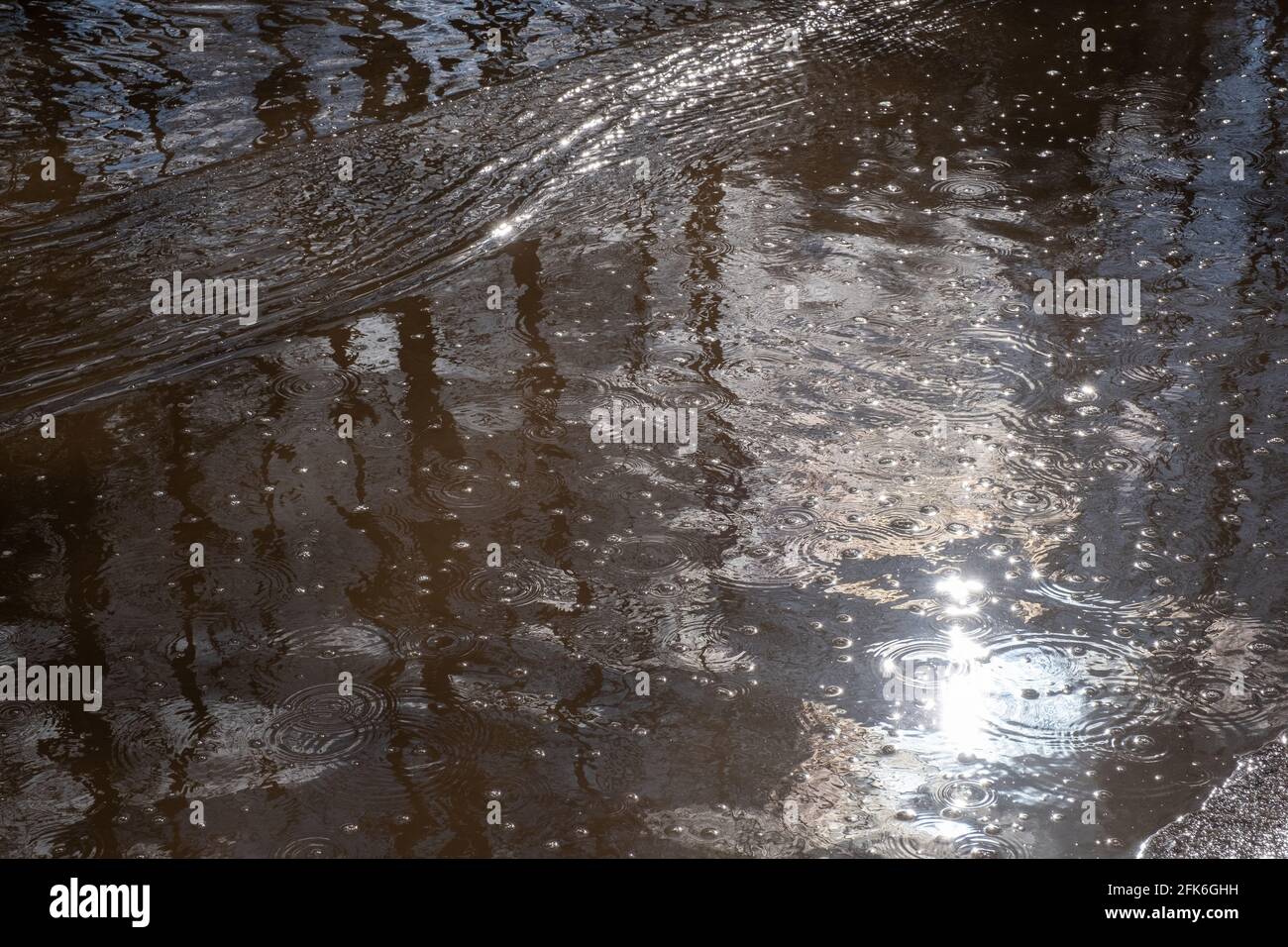 Bright sun glare and small waves on a spring puddle. An abstraction ...