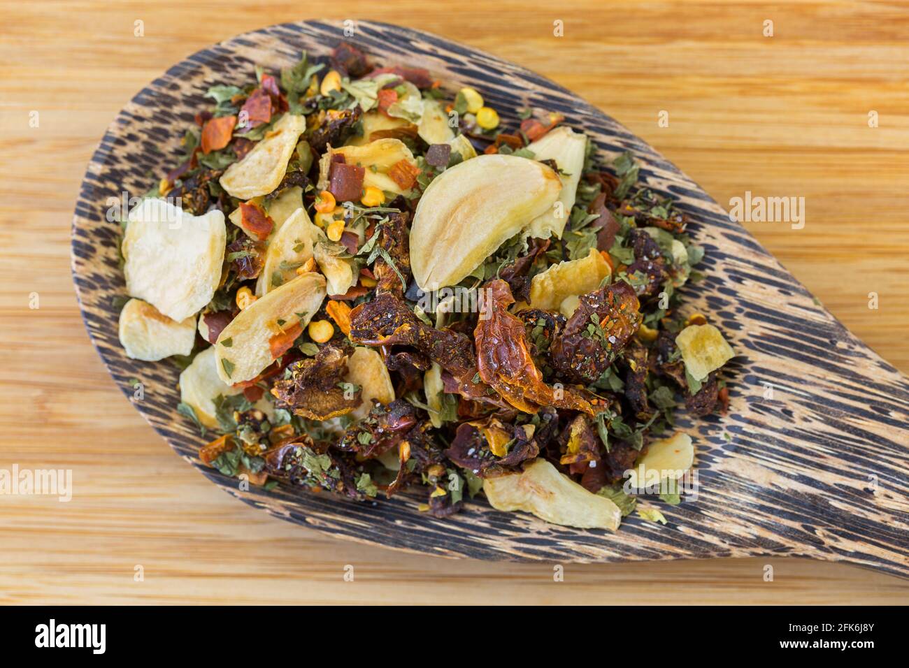 Wooden spoon of dried spicy red chili flakes, sliced garlic, parsley to ...