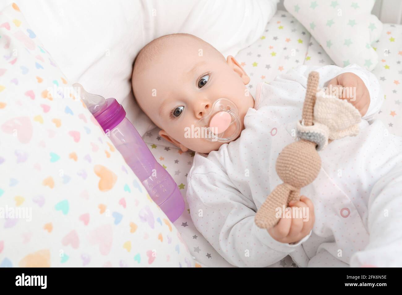 Cute little baby with bottle of water and toy in crib Stock Photo - Alamy