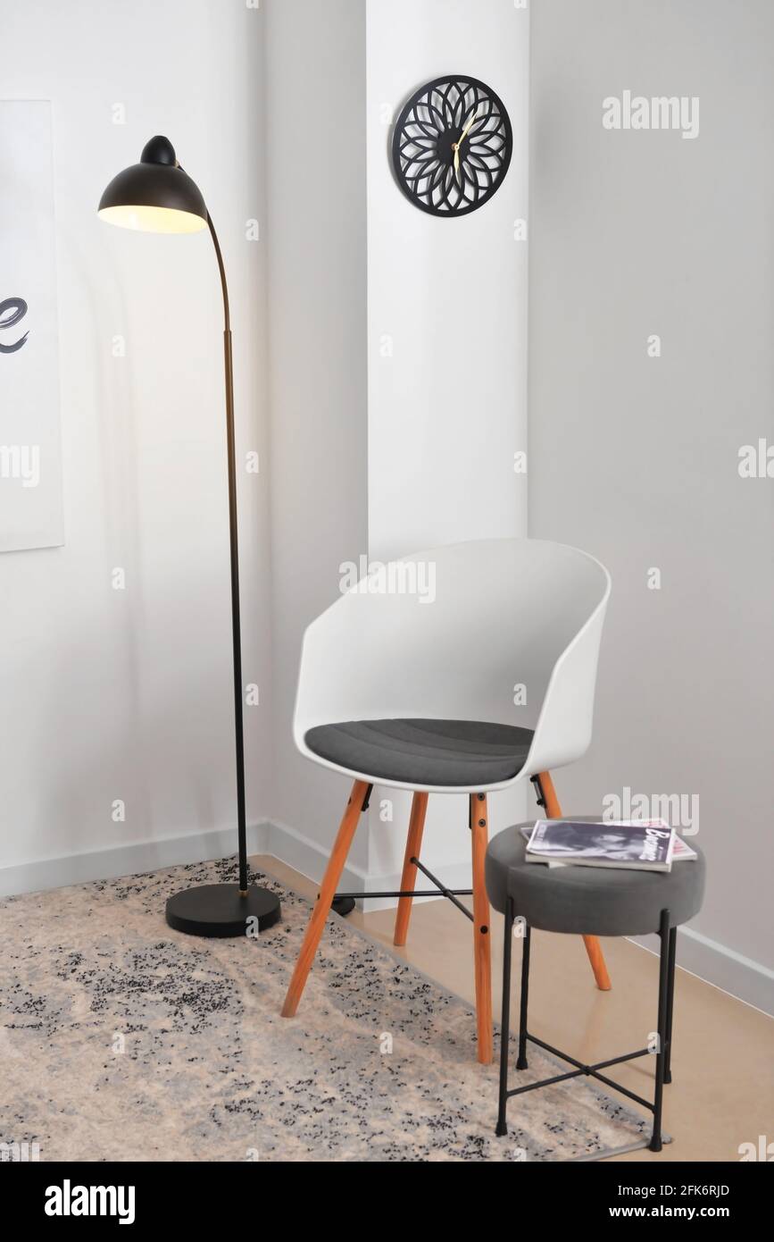 Modern chair and lamp near white wall in room Stock Photo - Alamy