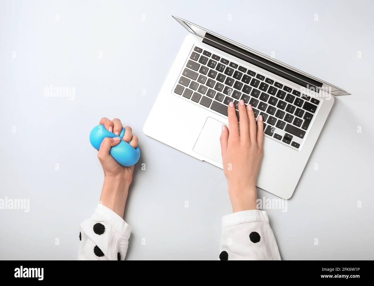 Woman squeezing stress ball while working with laptop on white ...