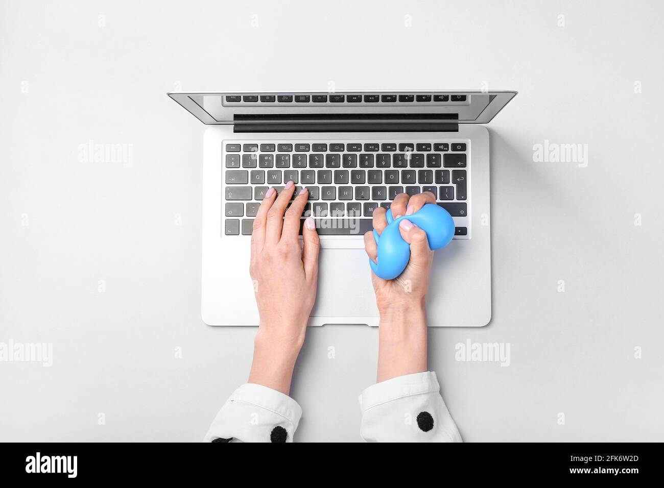Woman squeezing stress ball while working with laptop on white ...