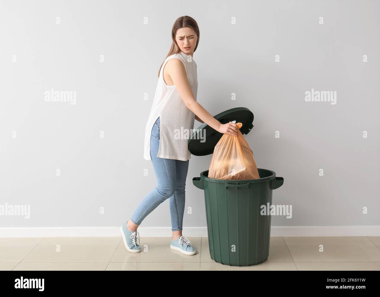 Young woman putting garbage in trash bin on light background Stock ...