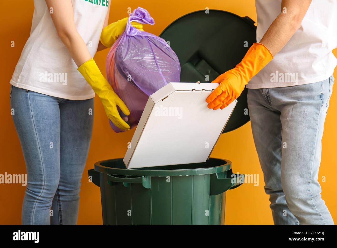 Volunteers putting garbage in trash bin on color background Stock Photo ...
