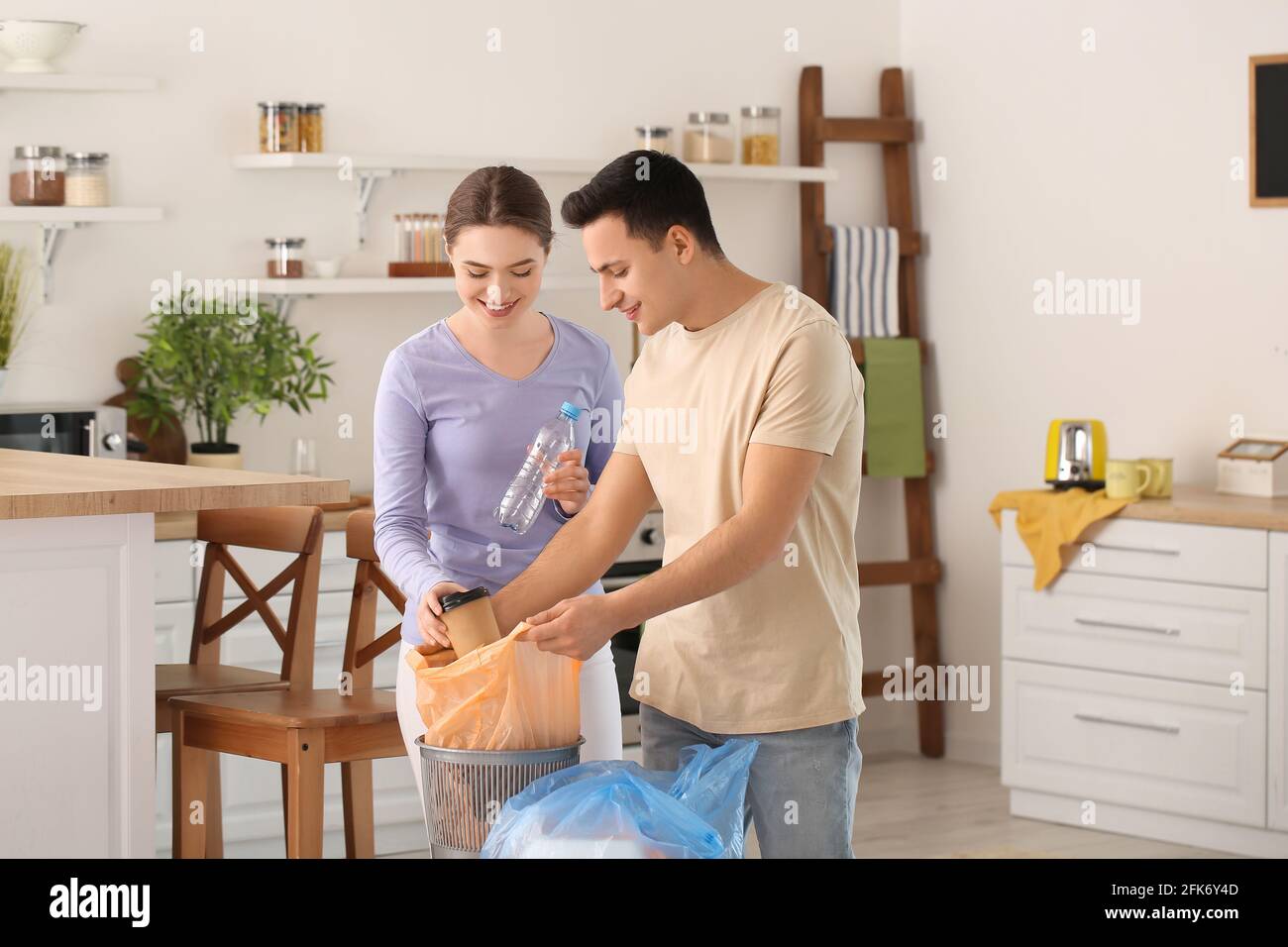 Young couple putting garbage in trash bin at home Stock Photo - Alamy