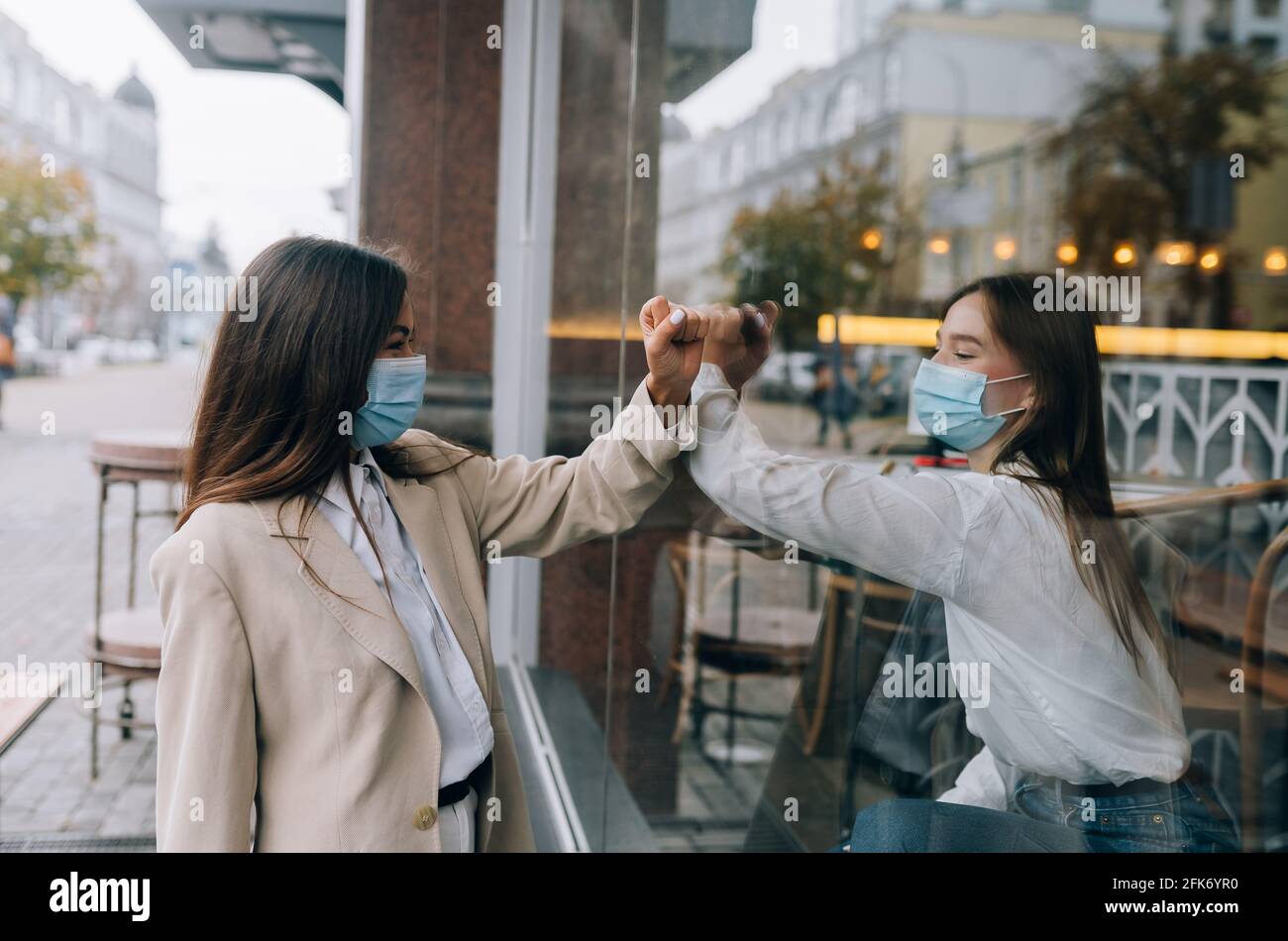 Two women in protective masks opposite each other, window between them ...
