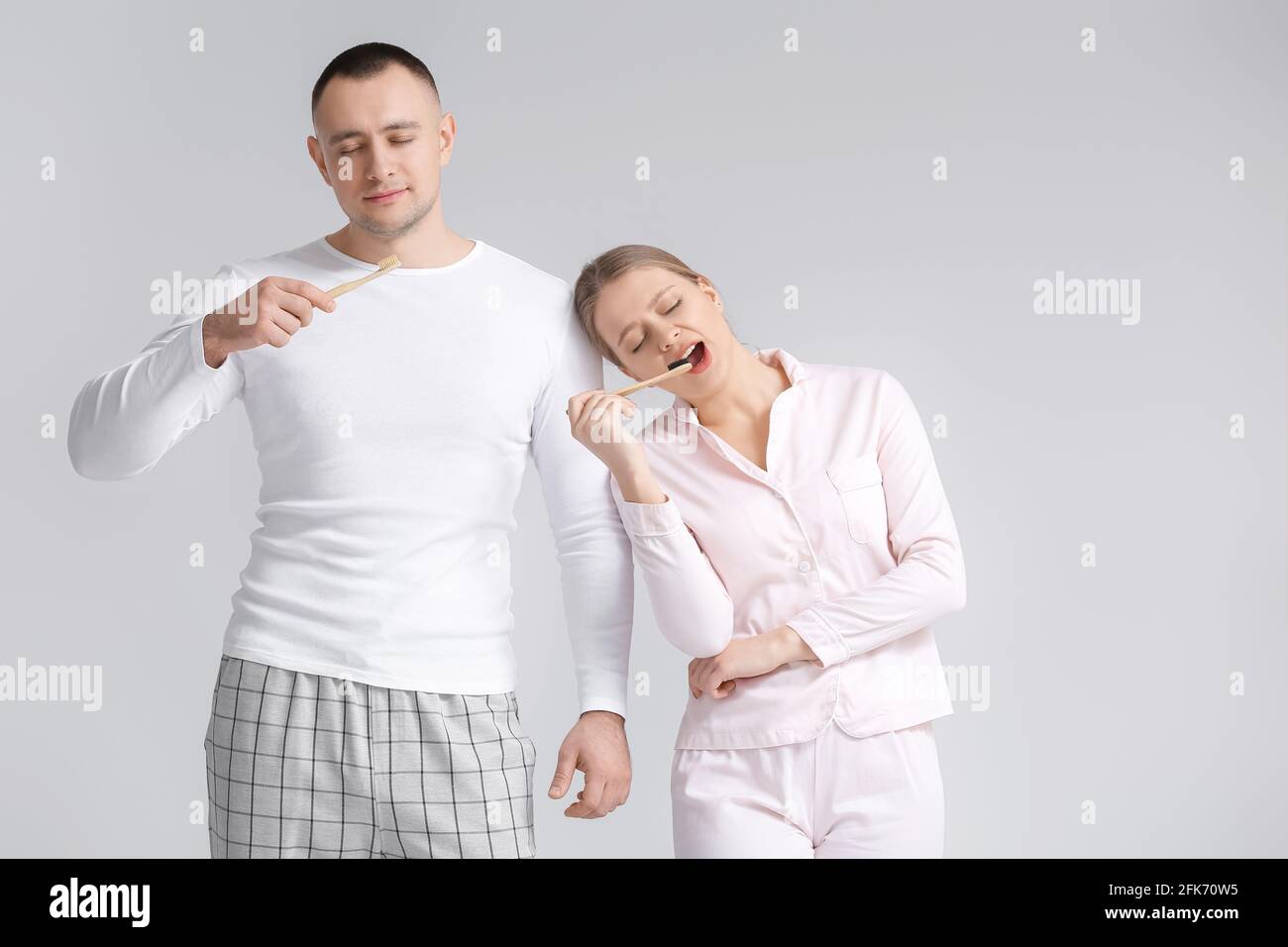 Sleepy young couple brushing teeth on grey background Stock Photo - Alamy