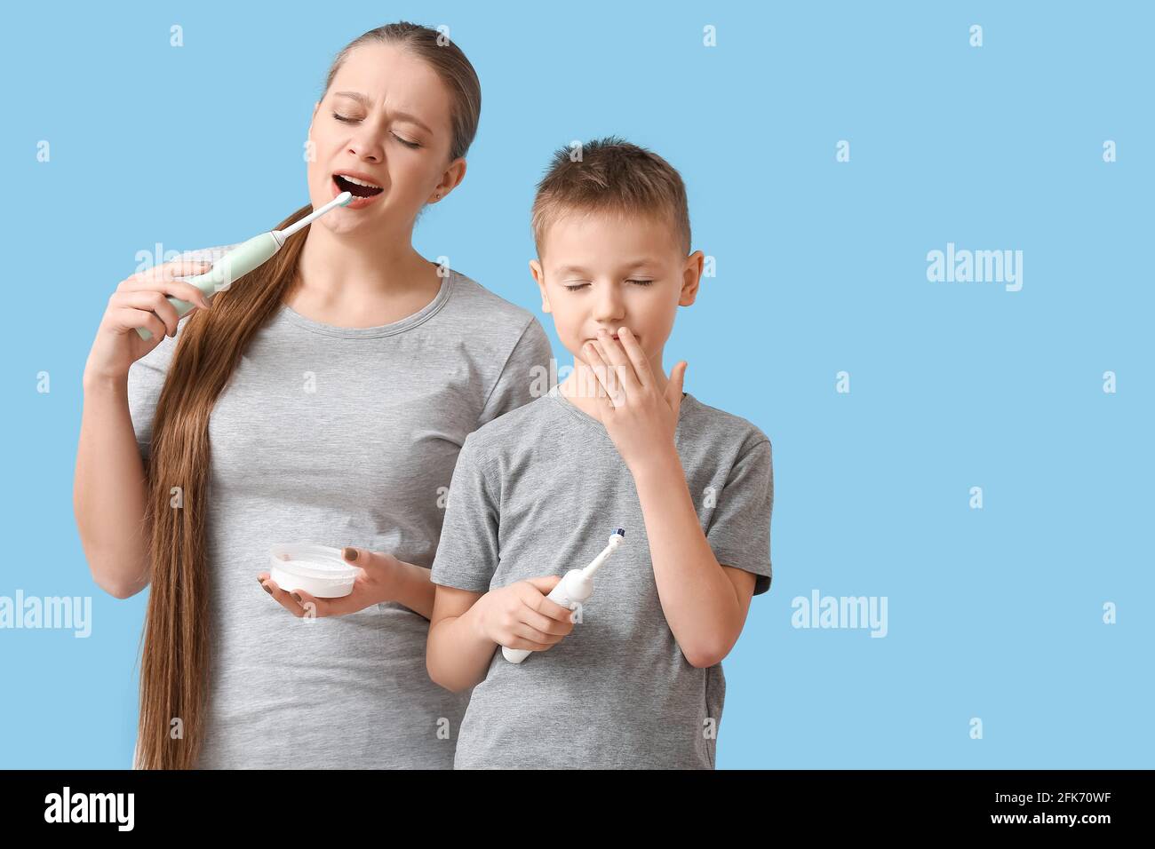 Sleepy mother and little son brushing teeth on color background Stock ...