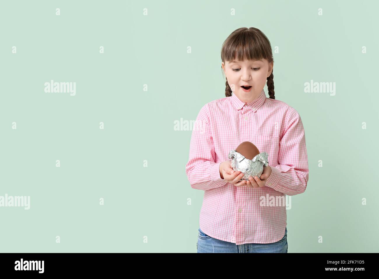 Surprised little girl with chocolate Easter egg on color background ...
