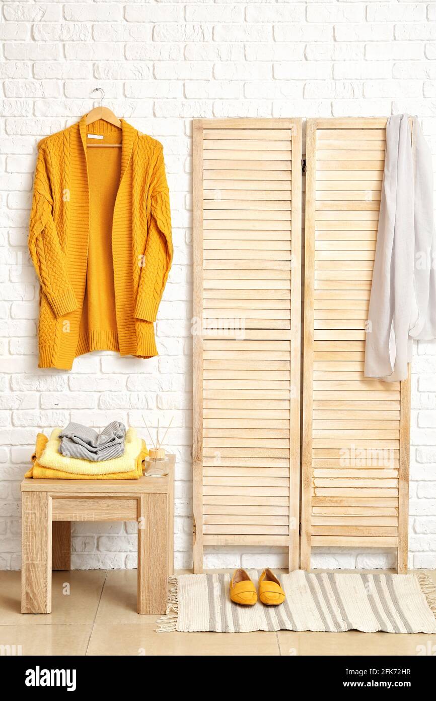 Folding screen and table with stylish clothes in modern room Stock ...