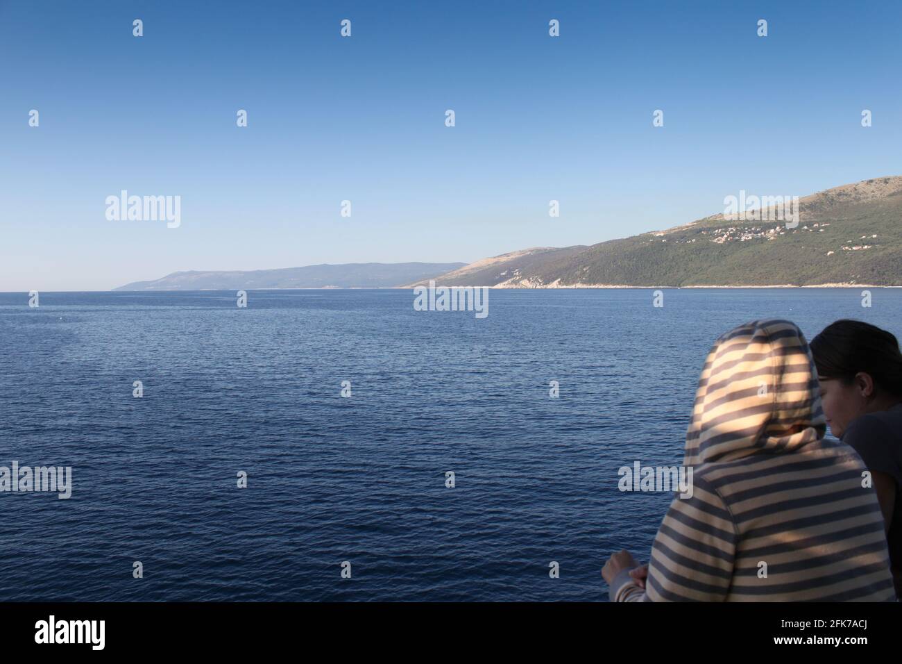 Two people watching the sea from a ferry boat on a summer morning . The ...
