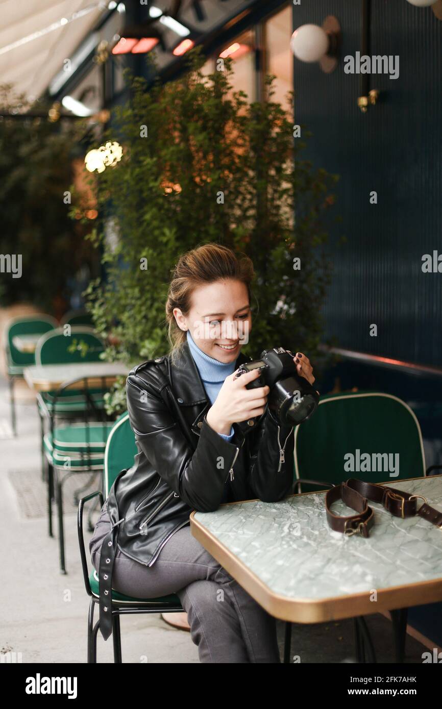Young caucasian woman sitting at street cafe with camera and looking at ...