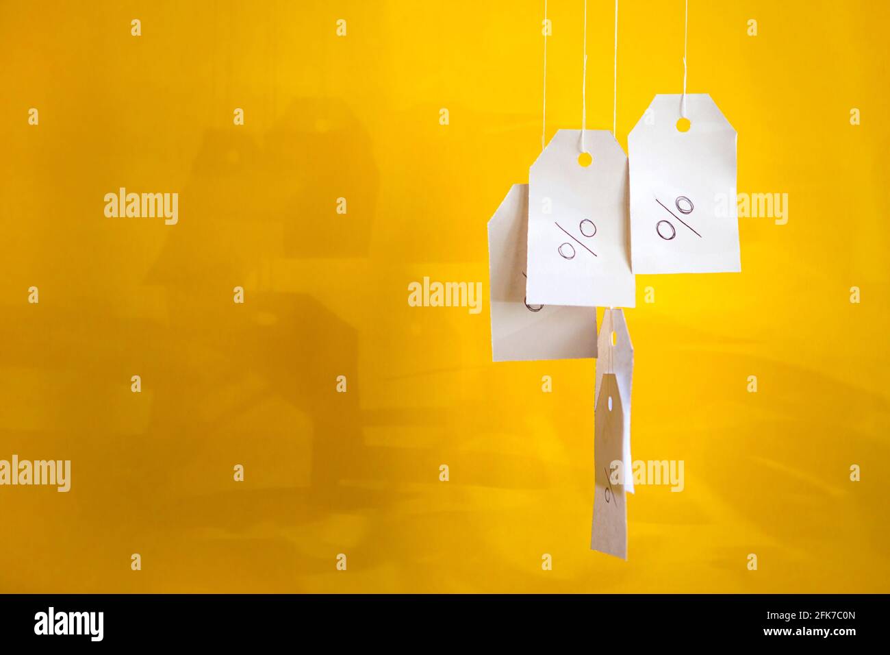 White tags with the percent sign hang on strings on a yellow background ...