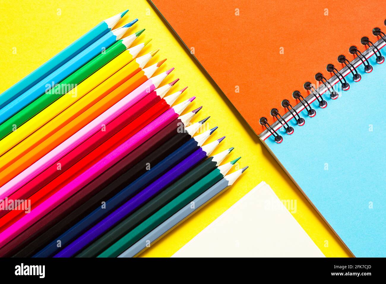 Rainbow palette of colored pencils with a spiral notebook on a yellow ...