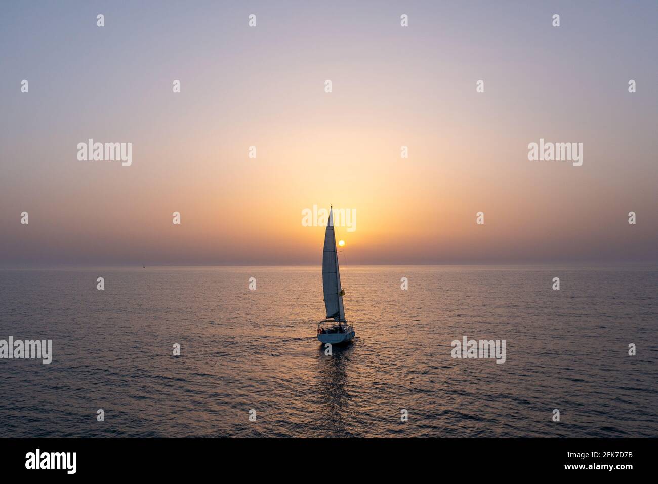 Sail boat sailing slowly towards a setting Sun in the Mediterranean Sea ...