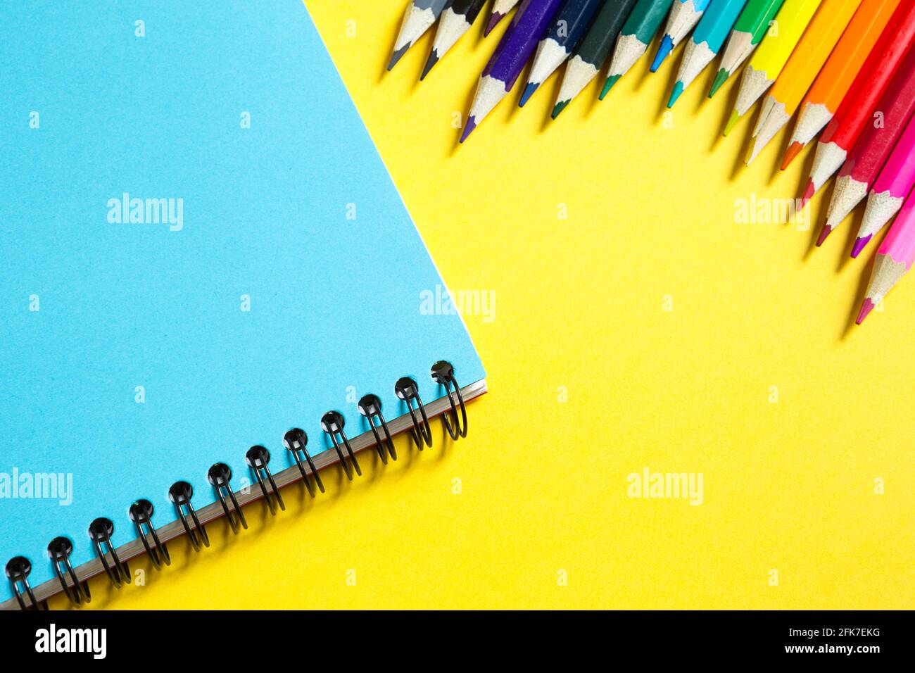 Rainbow palette of colored pencils with a spiral notebook on a yellow ...