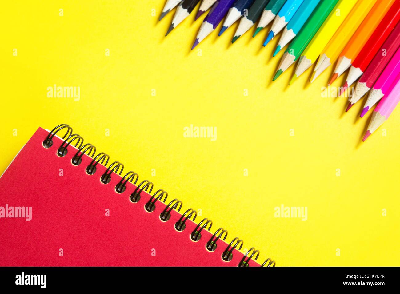Rainbow palette of colored pencils with a spiral notebook on a yellow ...