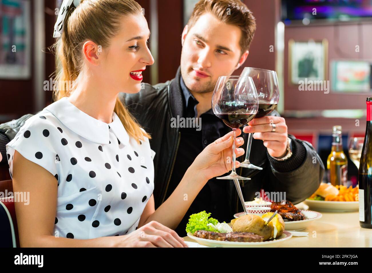 Young couple eating fast food and drinking red wine in a American retro ...