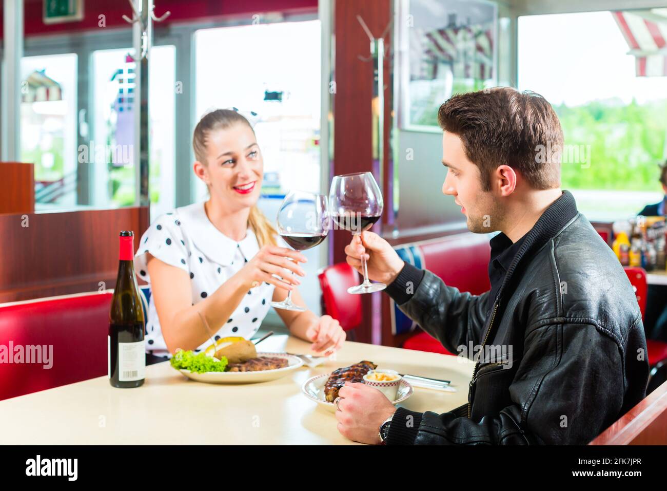 Young couple eating fast food and drinking red wine in a American retro ...
