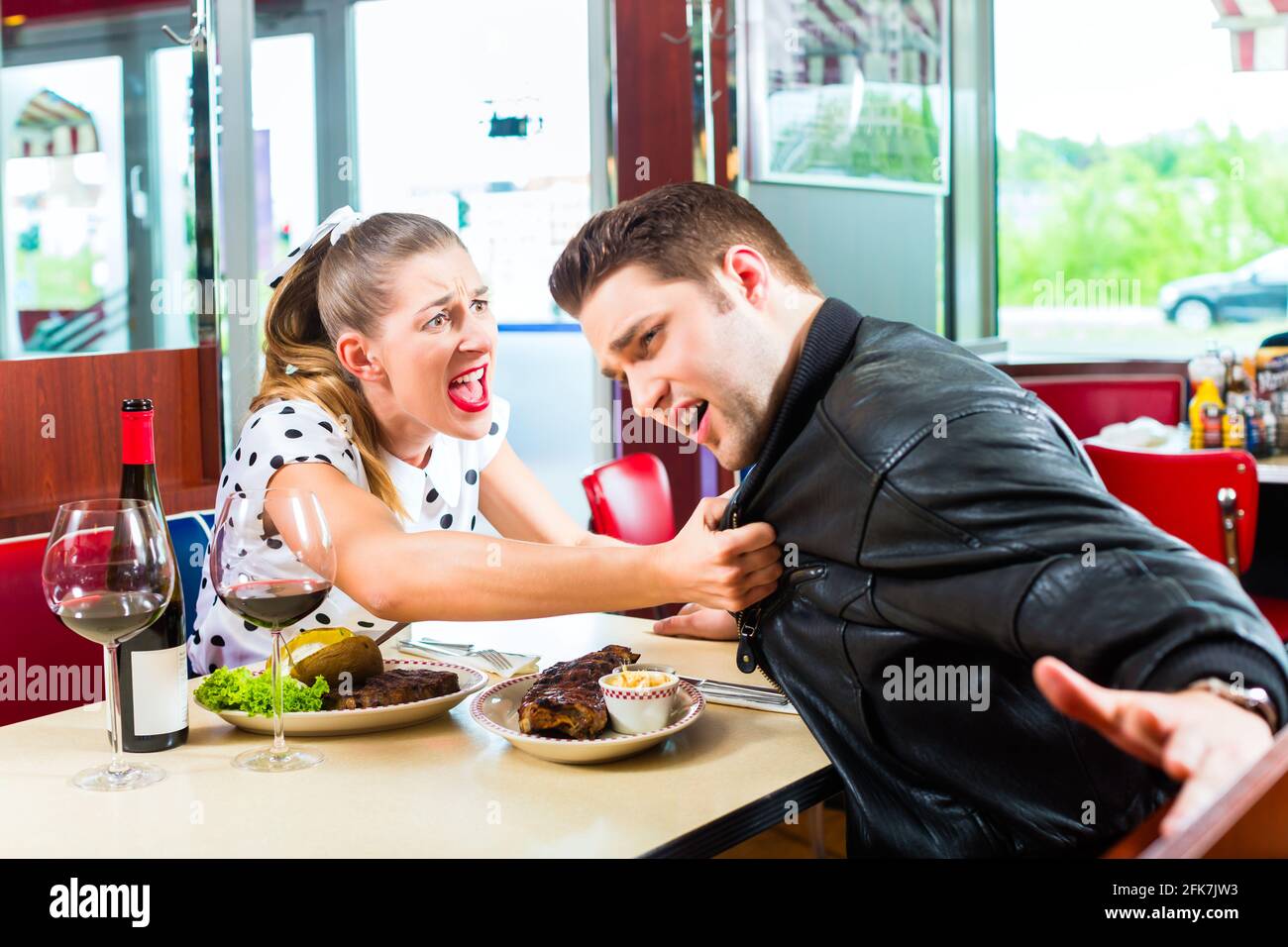 Young couple eating fast food and drinking red wine in a American retro ...