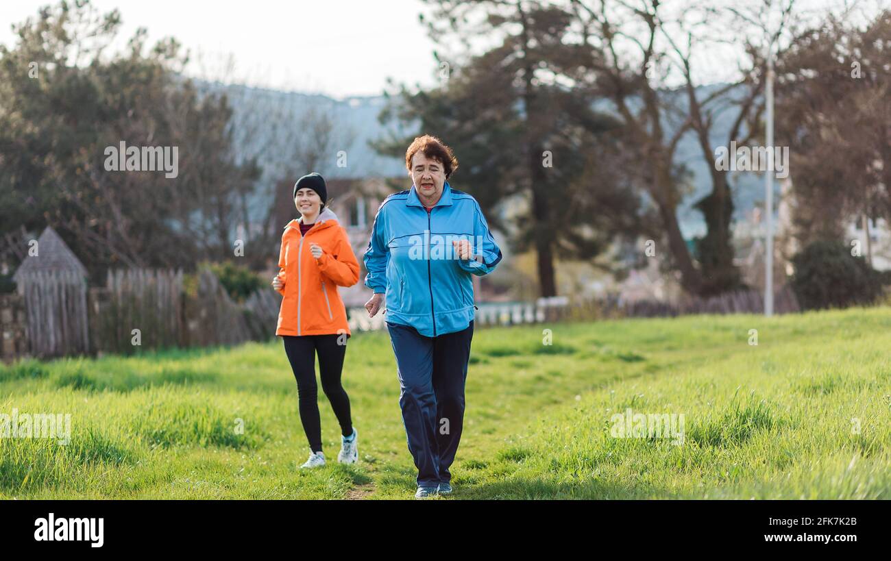 Elderly and young smiling women in sports clothes, running in the park ...