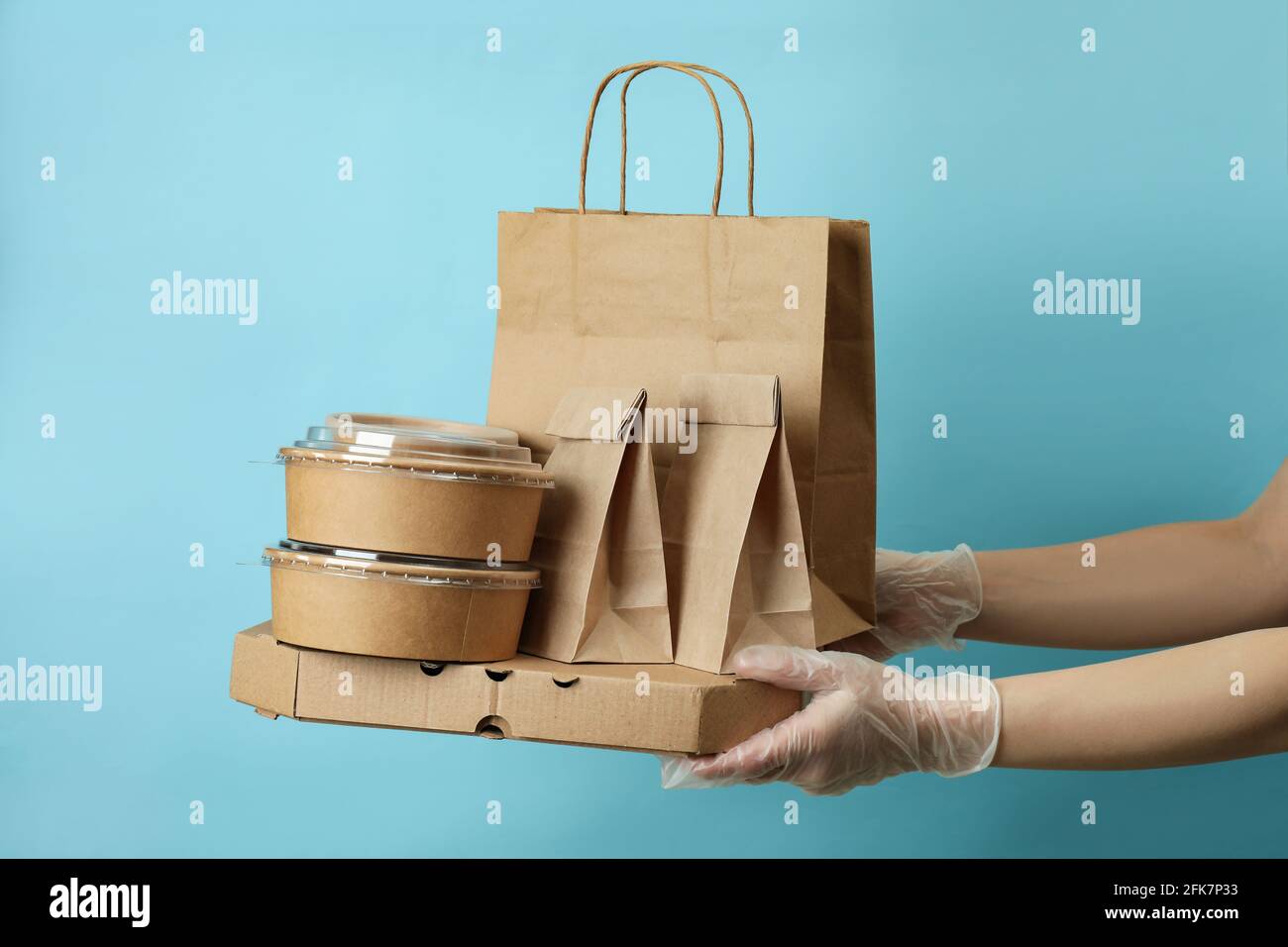 Hands in gloves hold delivery containers for takeaway food on blue ...