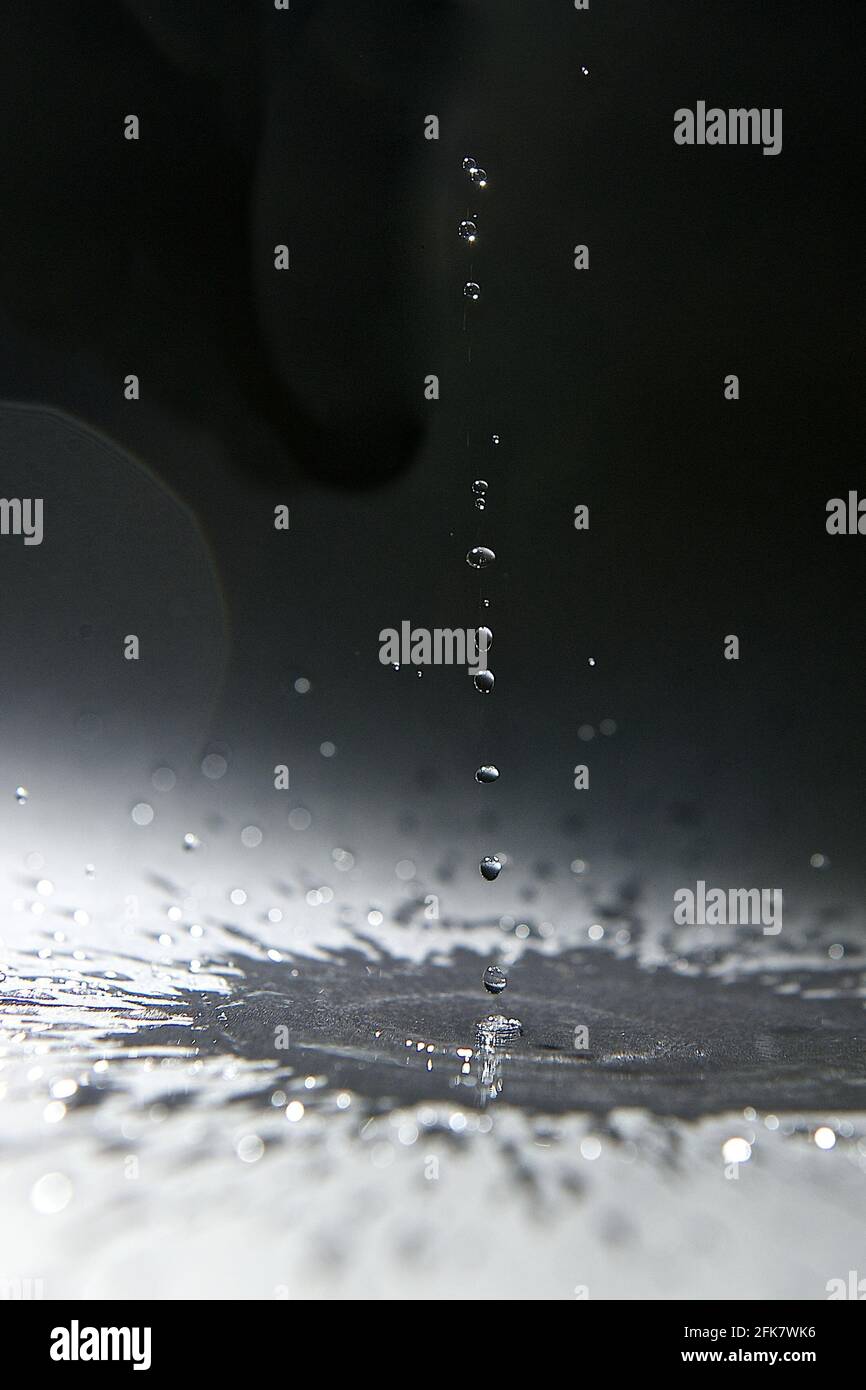 Vertical greyscale shot of drops of water dripping a surface Stock ...