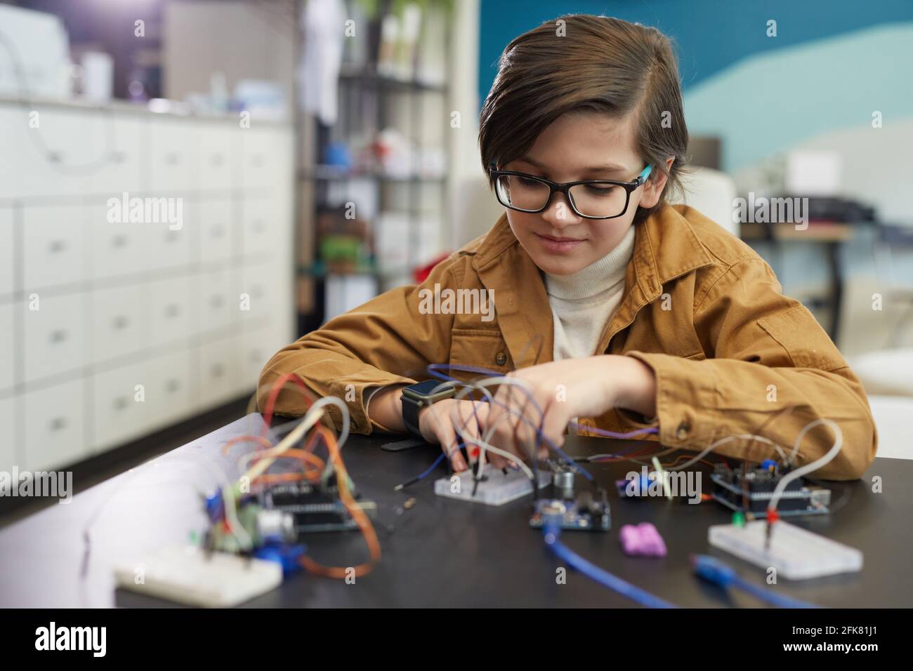 Portrait of cute boy wearing glasses and working with electric circuits ...