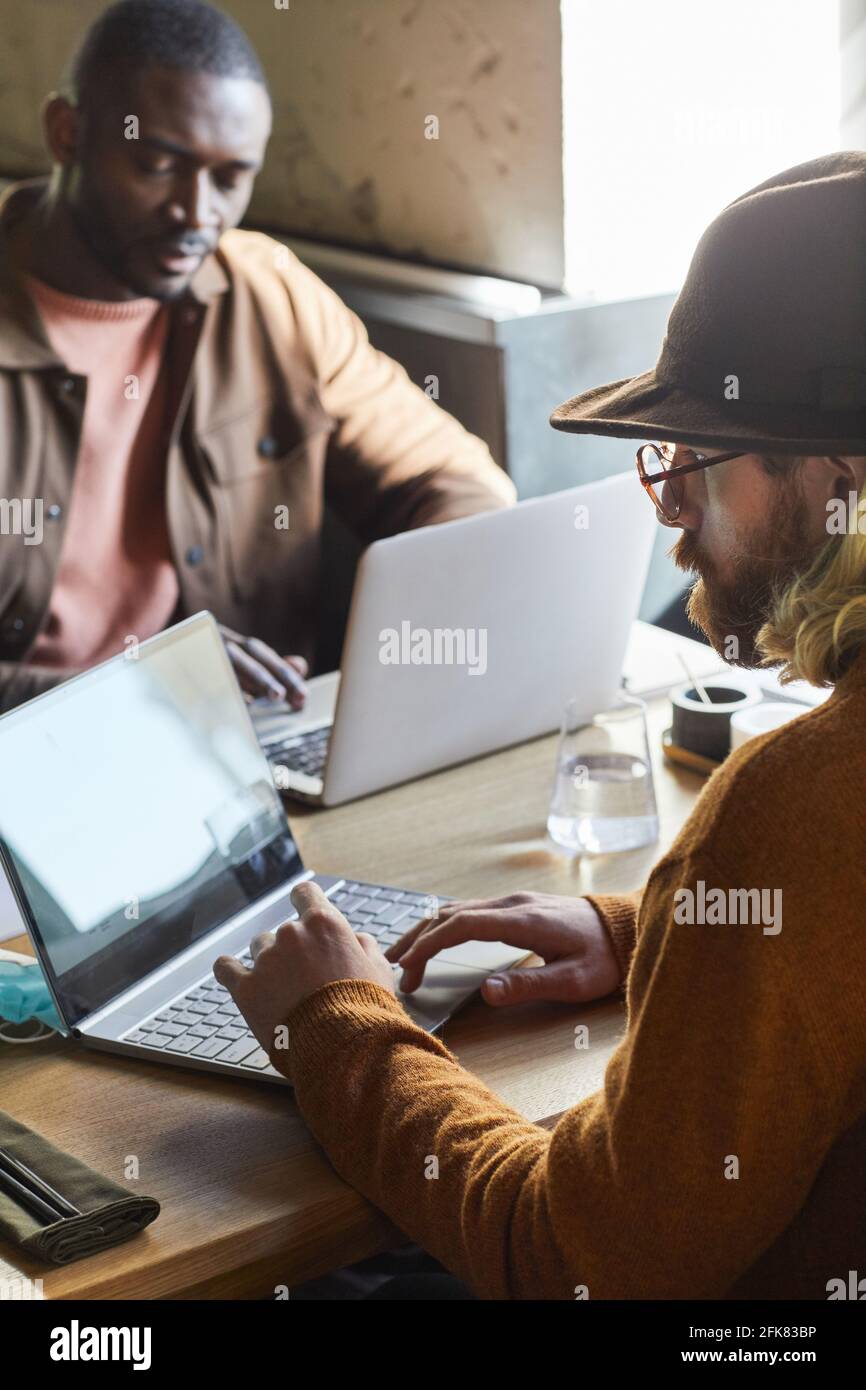 Vertical portrait of two contemporary men using laptops while working ...