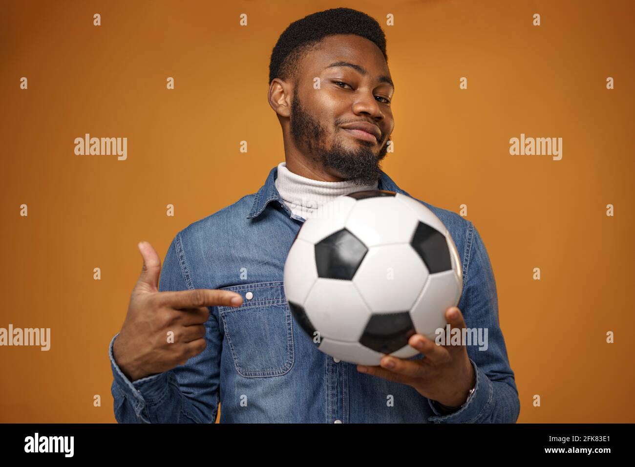 African american man holding soccer ball and pointing on it, yellow ...