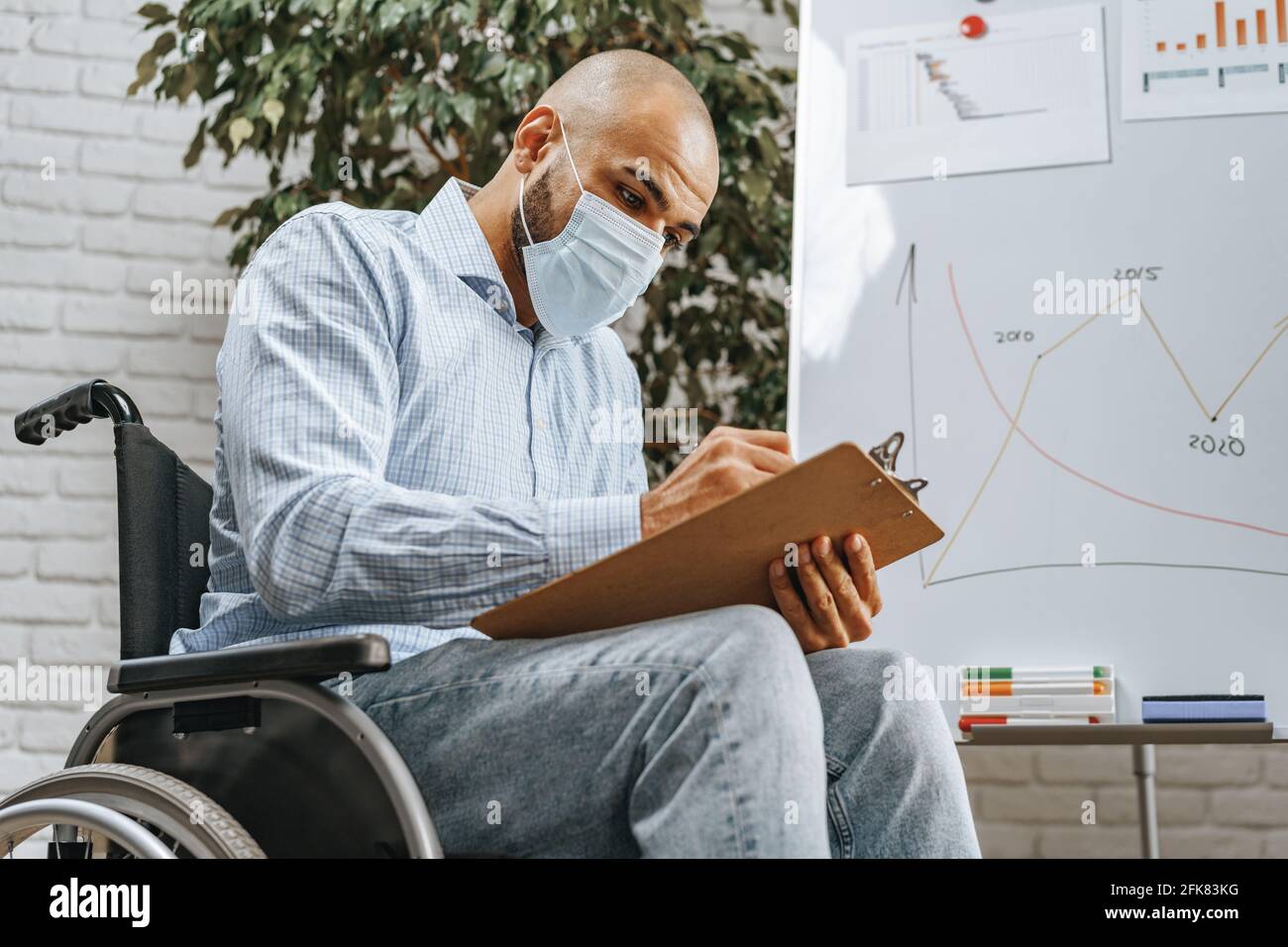 Disabled young man making presentation in office wearing medical mask ...