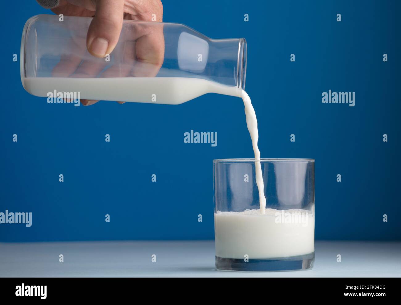 glass of milk half full, hand with overturned glass bottle, blue ...