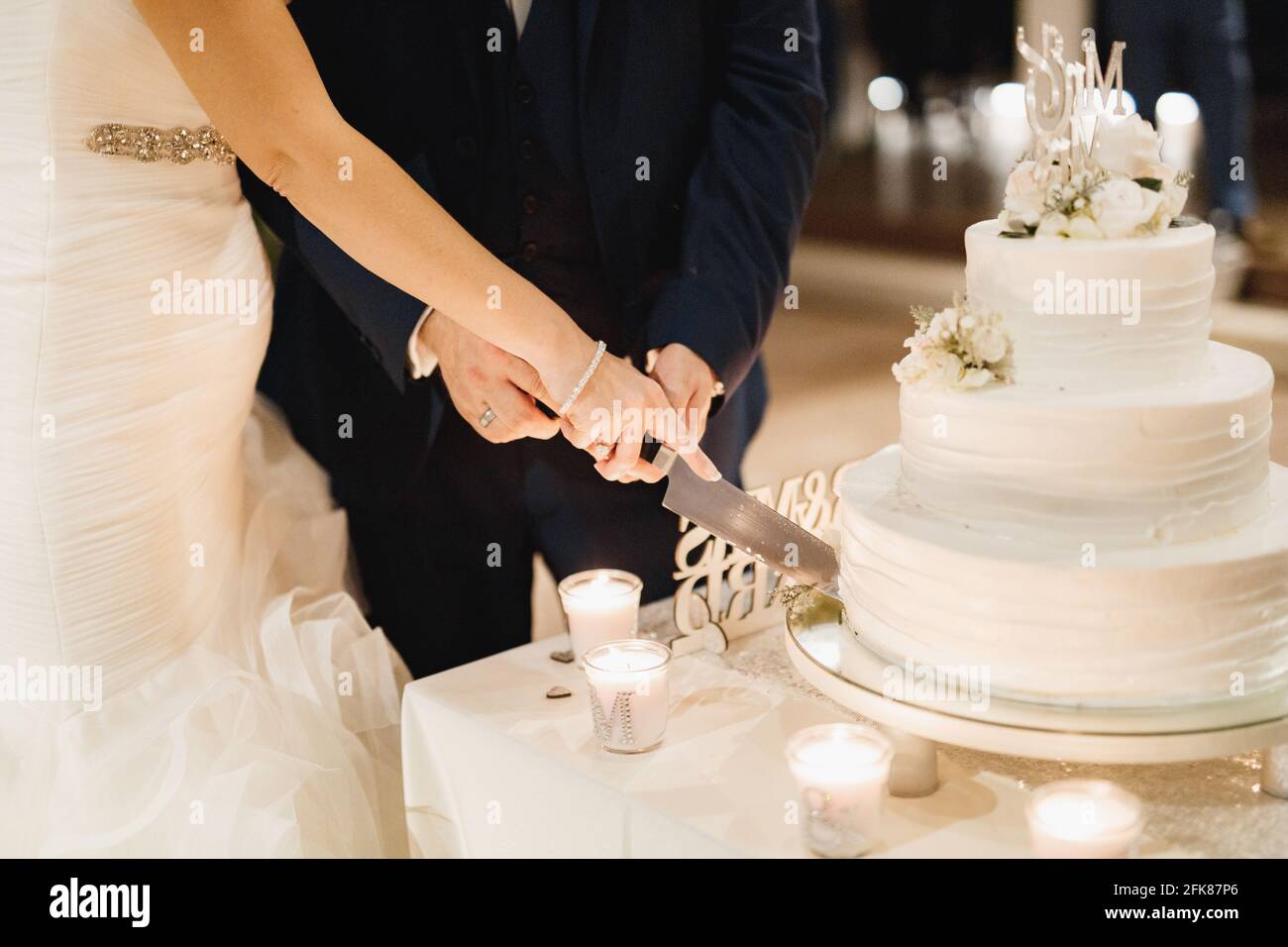 Bride and groom cutting three-tiered cake in white frosting together at ...