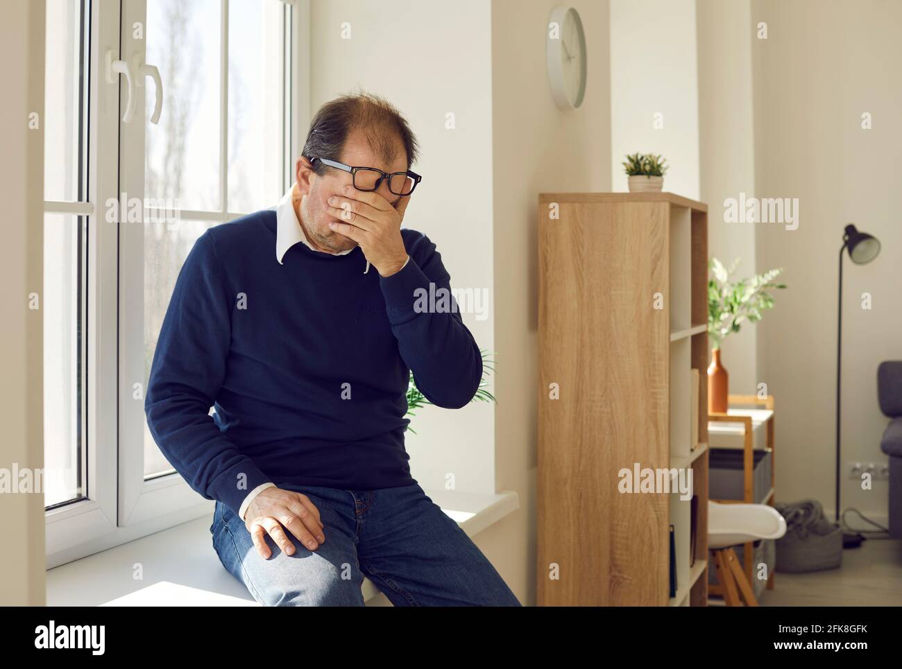Desperate mature man sitting alone on a windowsill and crying over life ...