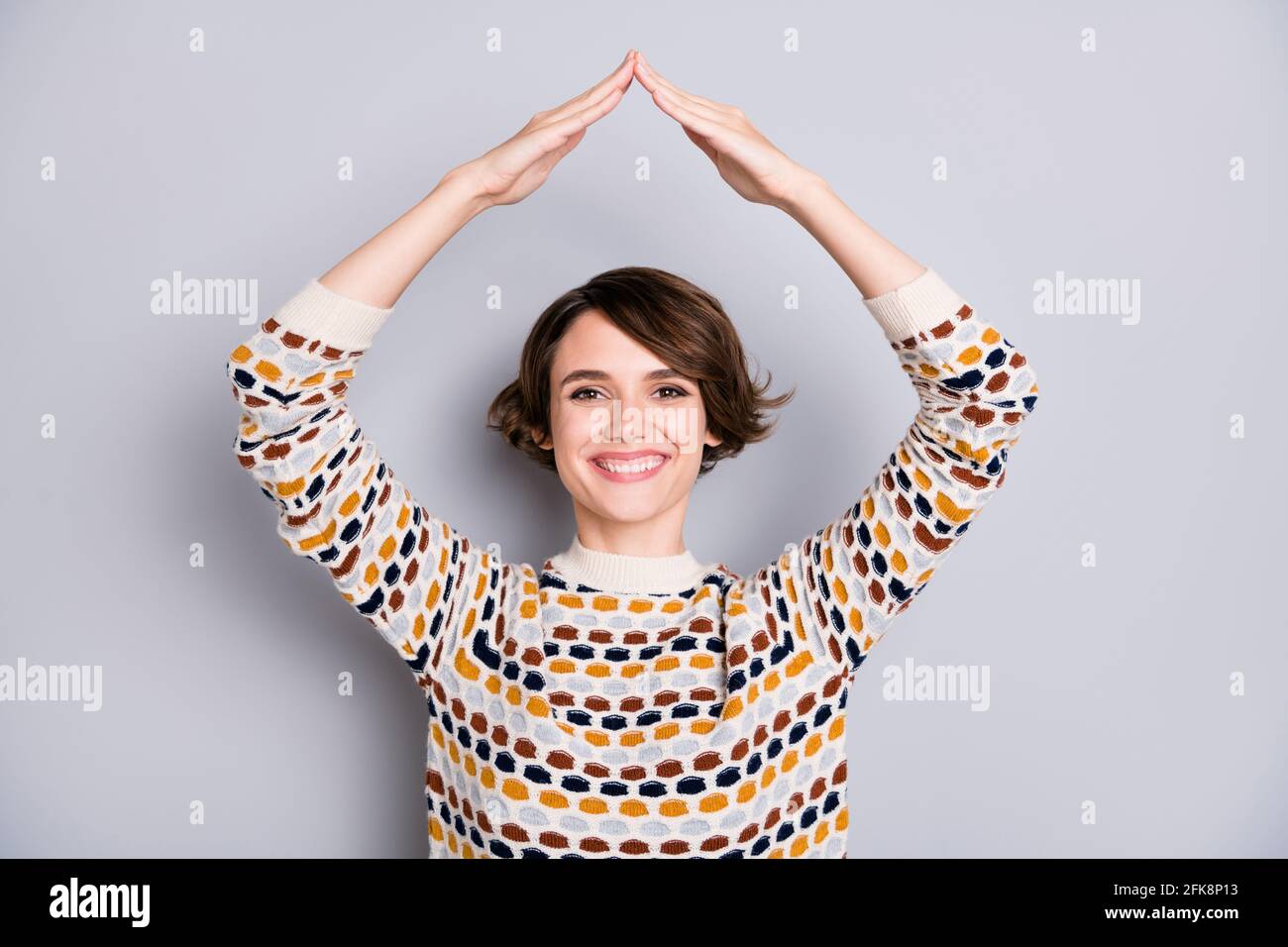 Portrait of attractive cheerful girl holding over head hands like roof ...