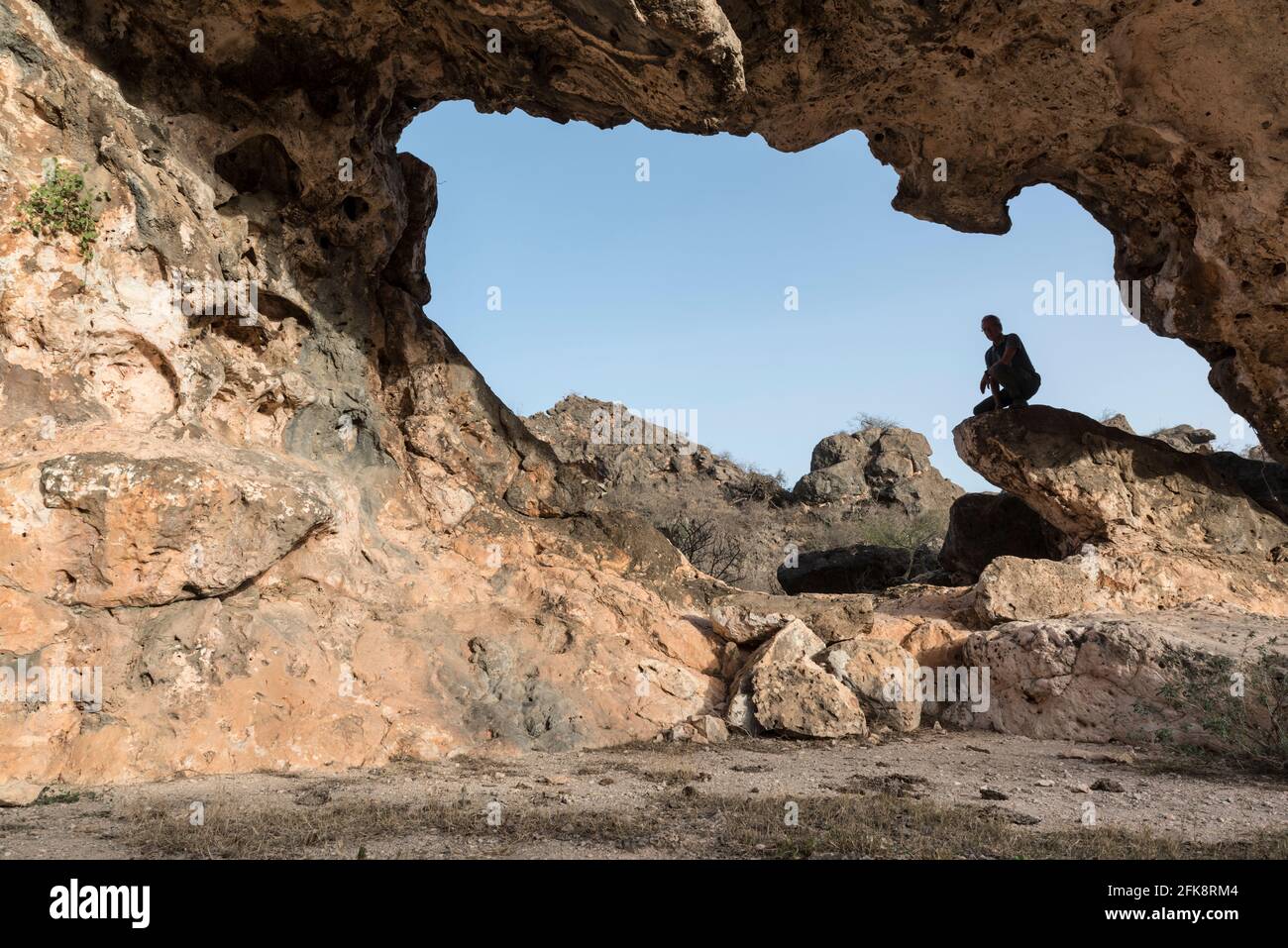 Male person kneeling in an opening of the rocks around Fazaya Beach ...