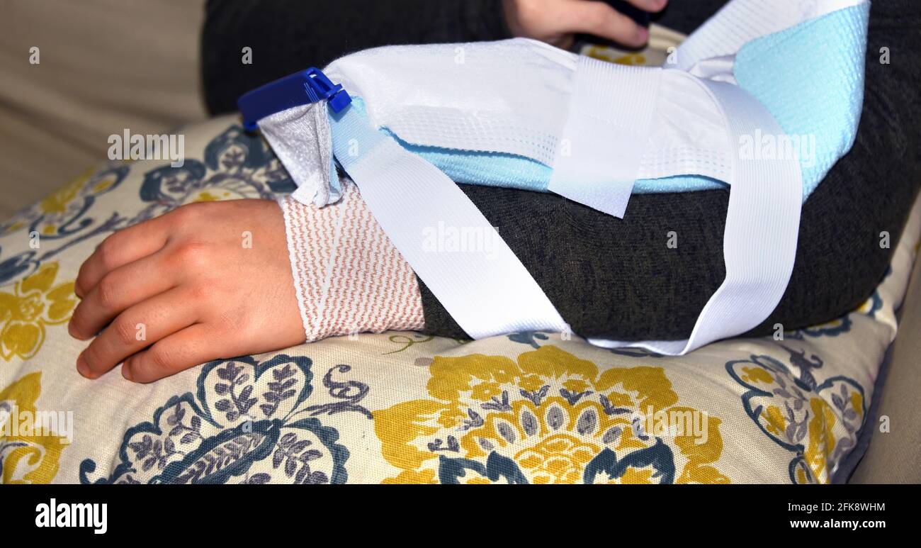 Little girl sits with an ice pack on her arm injury. She is resting it ...