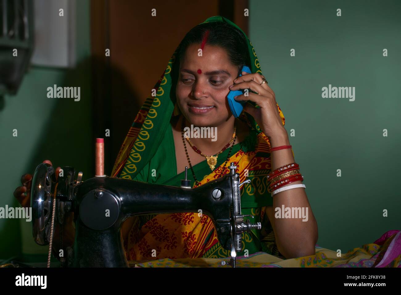 Indian rural woman using sewing machine and talking on a mobile phone ...