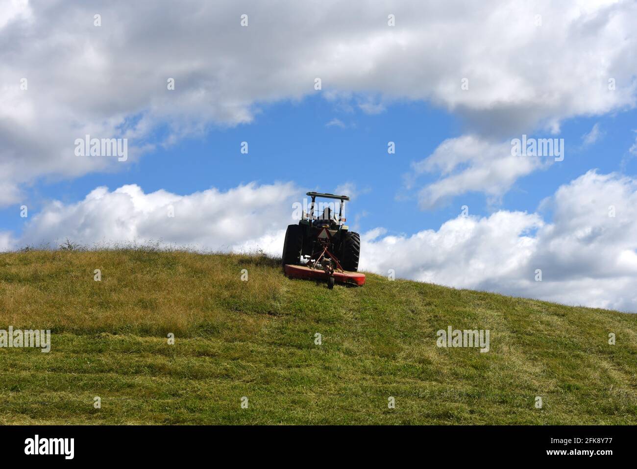 Man tops the hill with his tractor, in a field, in Tennessee. He is ...