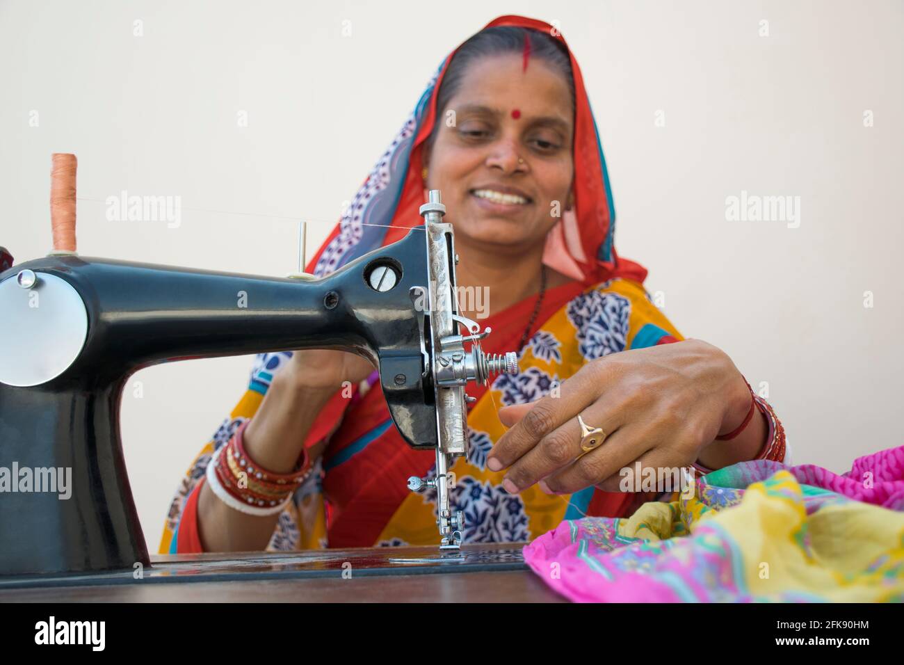 woman on a sewing machine making clothes in a rural indian village ...