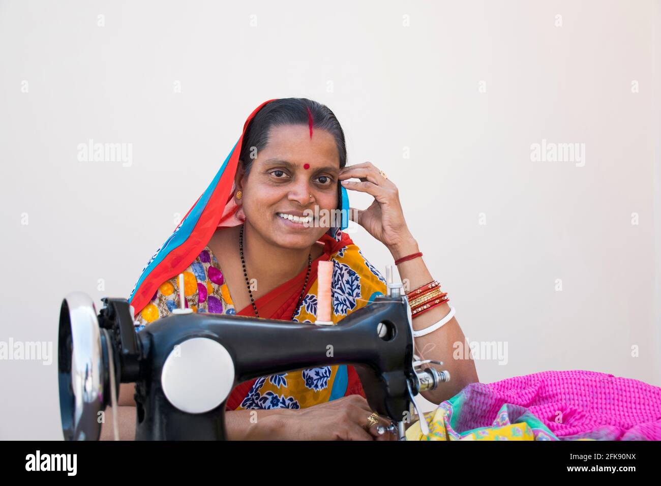 Indian rural Woman using sewing machine and talking on a mobile phone ...