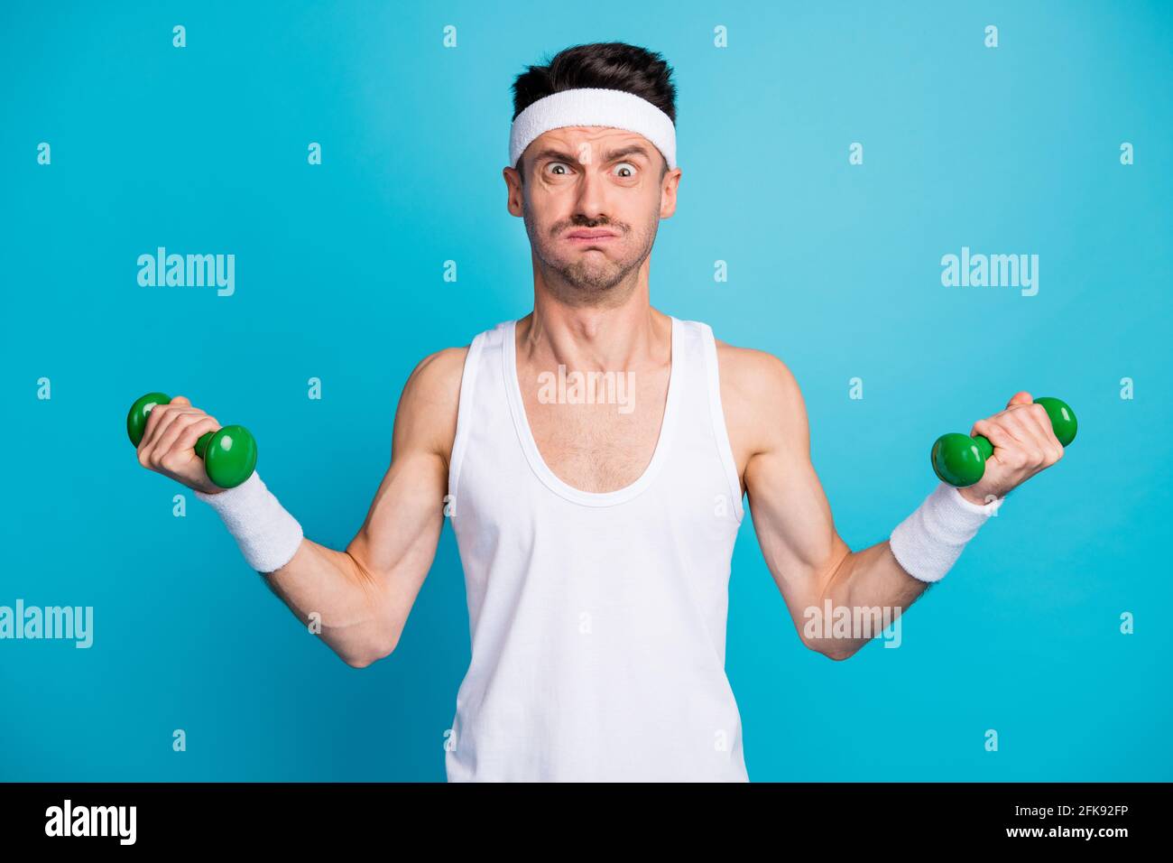 Photo of young sportsman exercise with heavy dumbells pouted cheekbones ...