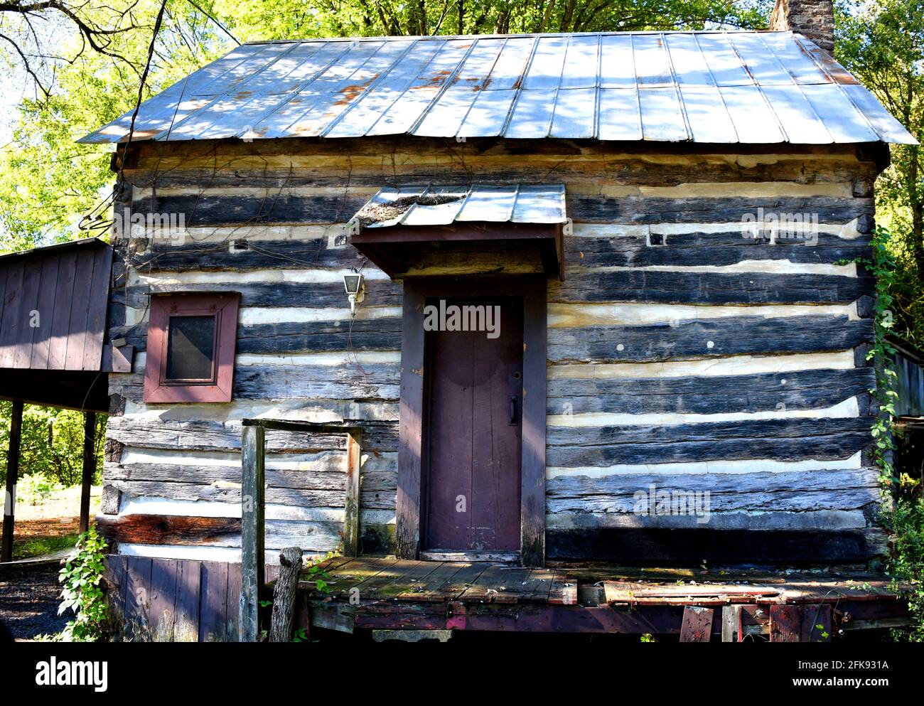 Old, rustic log cabin has a rotting front porch and a brown door ...