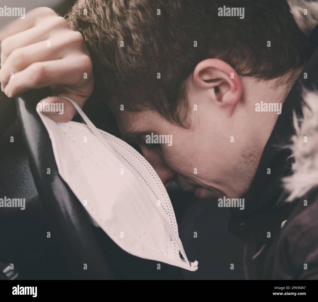 young tired man in a car, looking worried, holding a medical mask in ...
