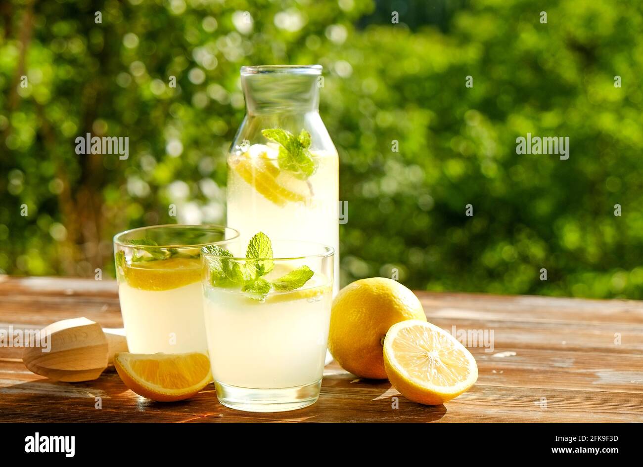 Lemonade pitcher, juicer, two glasses full of ice cold refreshing citrus beverage with lemon ...