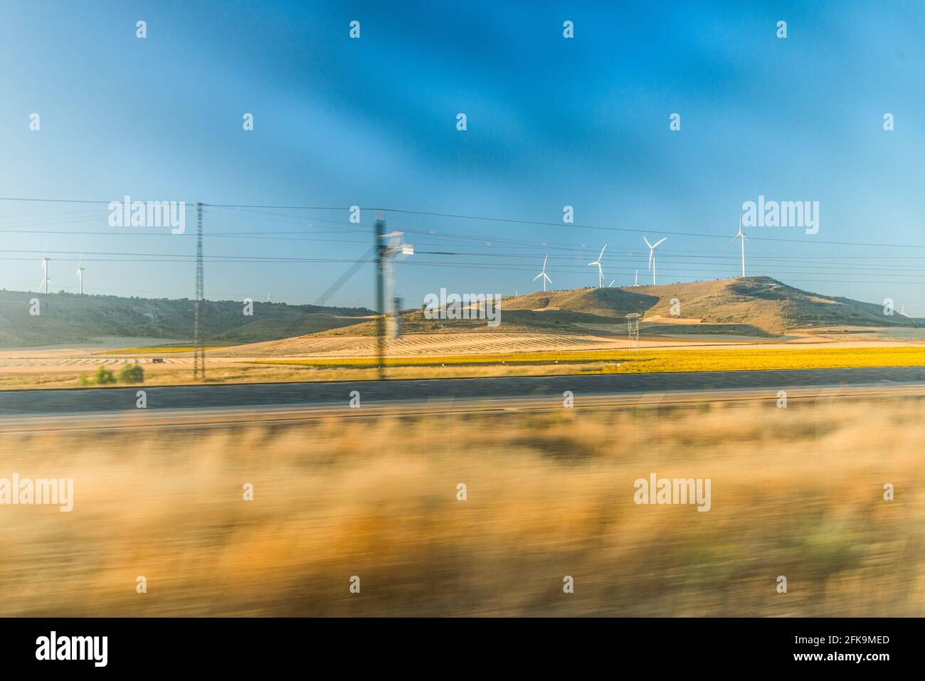Speeding across train tracks looking out over sunny fields. Wind farms ...